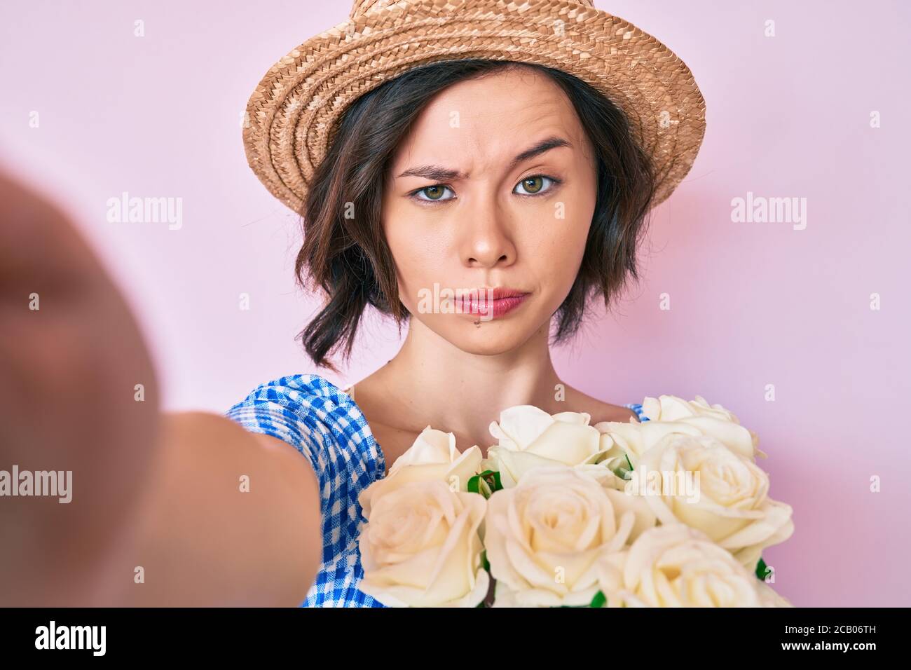 Young beautiful girl wearing summer hat taking a selfie skeptic and ...