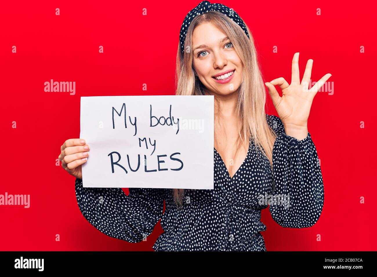 Young blonde woman holding my body my rules banner doing ok sign with ...