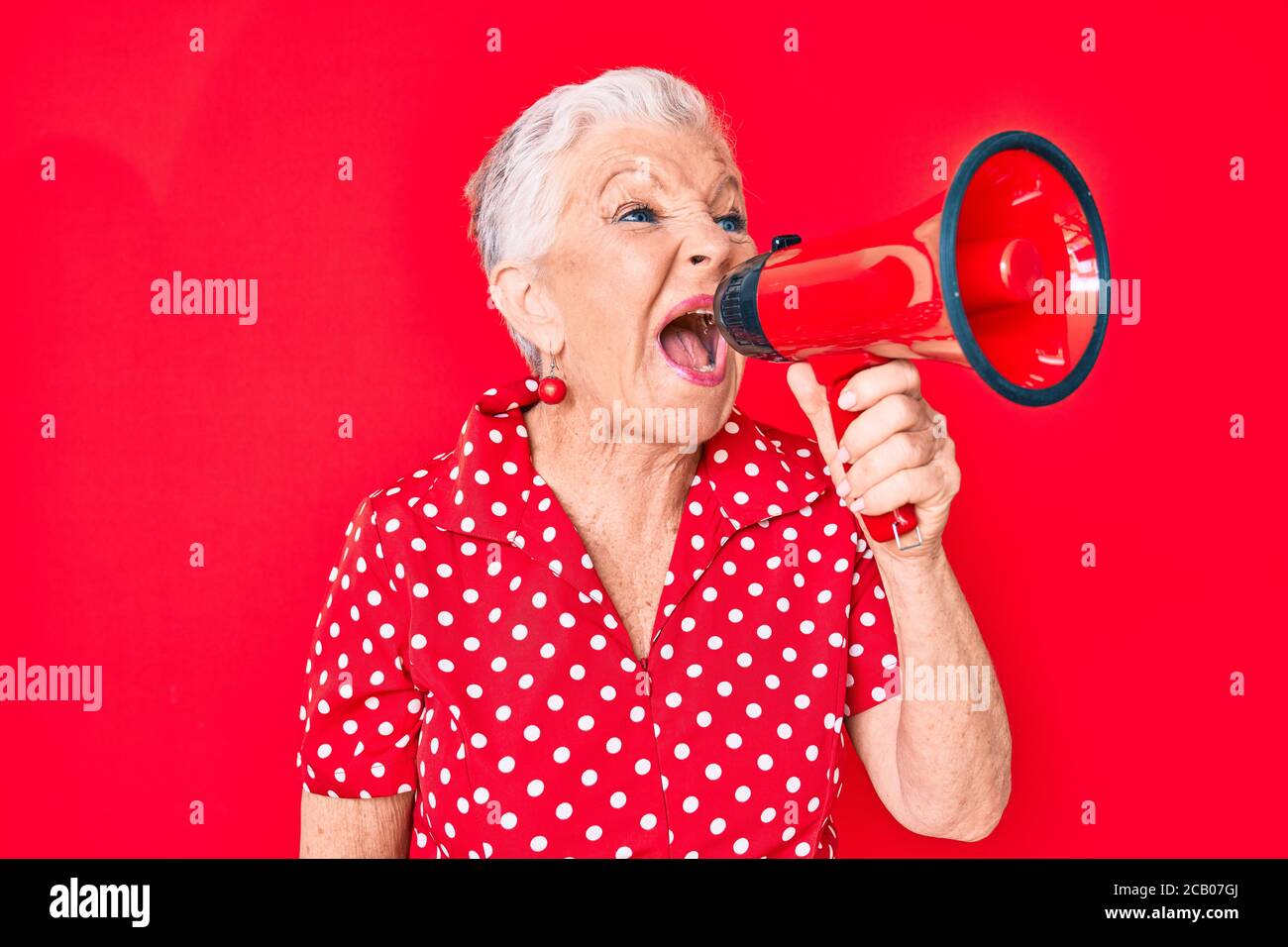 Senior beautiful grey-haired woman screaming using megaphone over ...