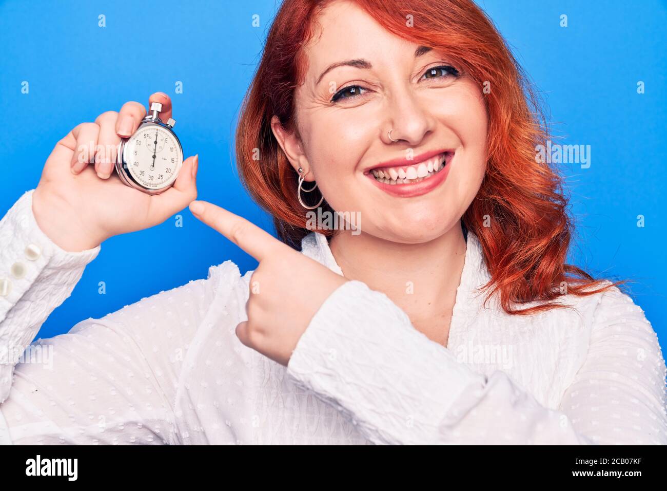 Young beautiful redhead woman doing countdown using stopwatch over blue ...