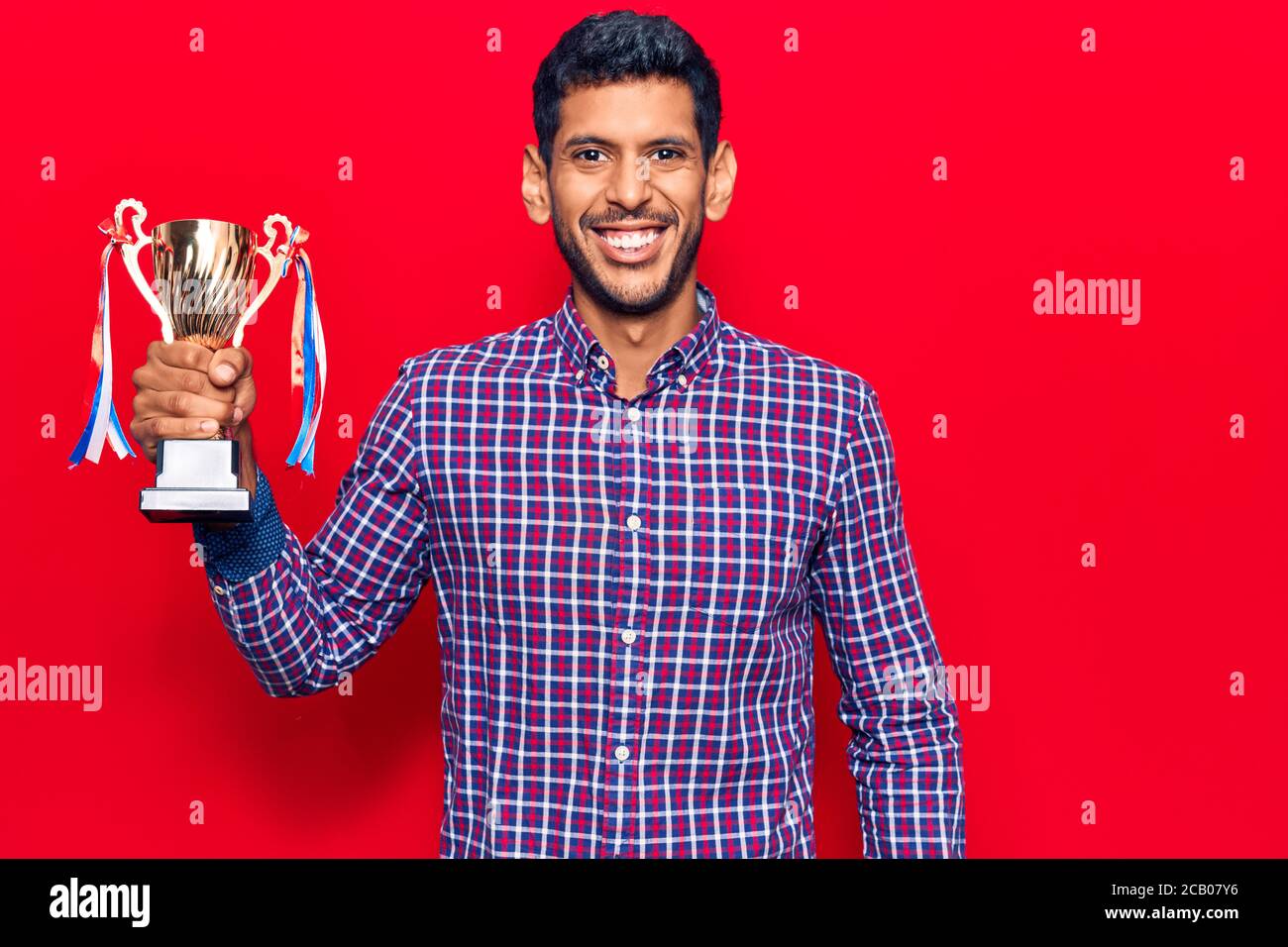 Young latin man holding winner trophy looking positive and happy ...