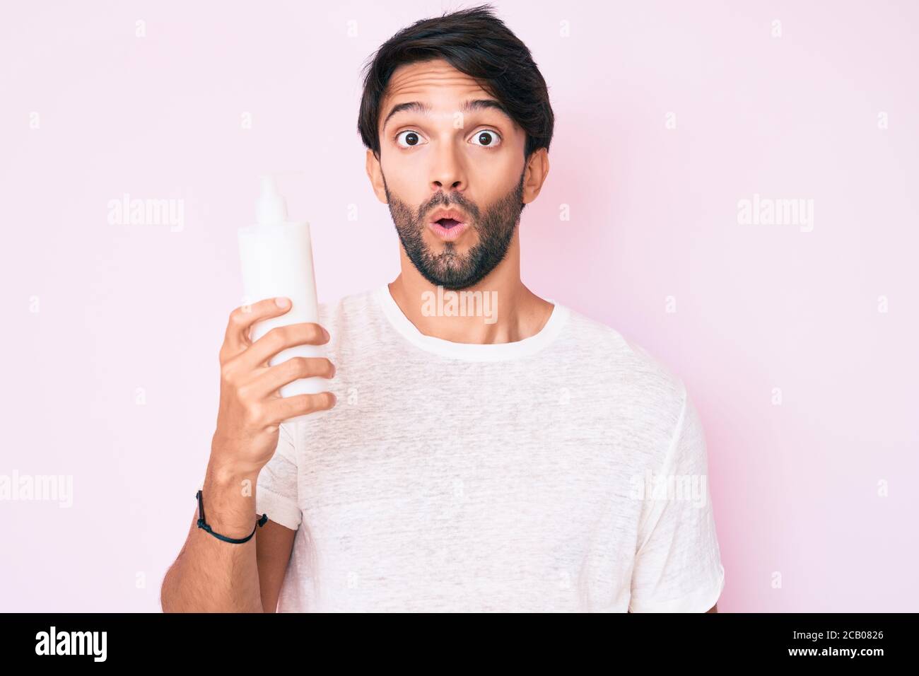 Handsome hispanic man holding cosmetic moisturizer facial cream scared ...