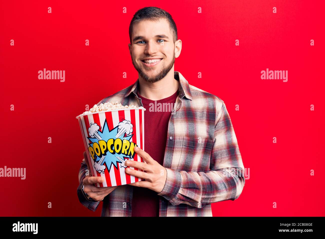 Young handsome man eating popcorn looking positive and happy standing ...