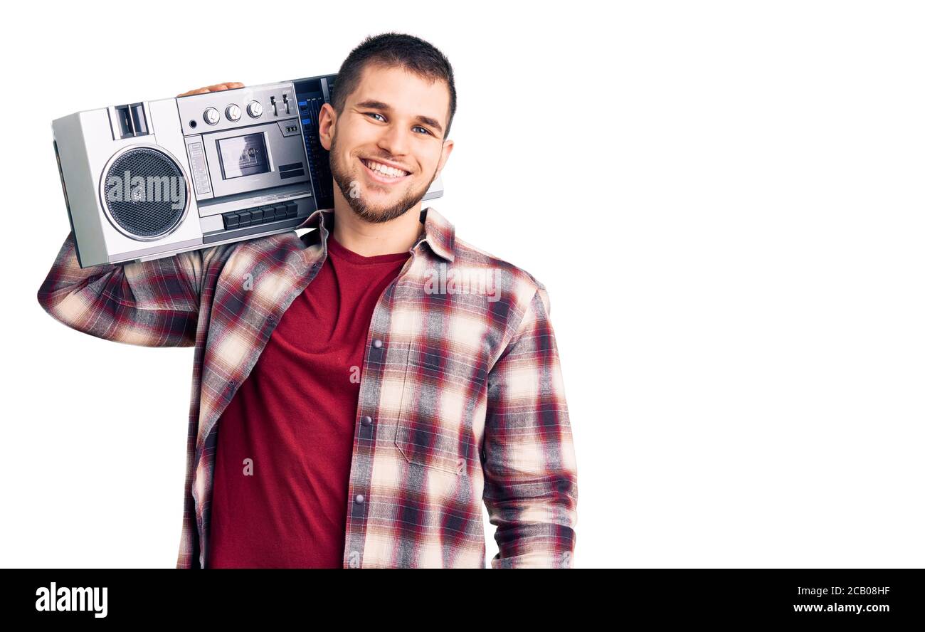 Young handsome man listening to music holding boombox looking positive ...