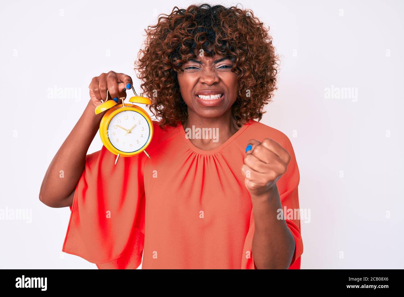 Young african american woman holding alarm clock annoyed and frustrated ...