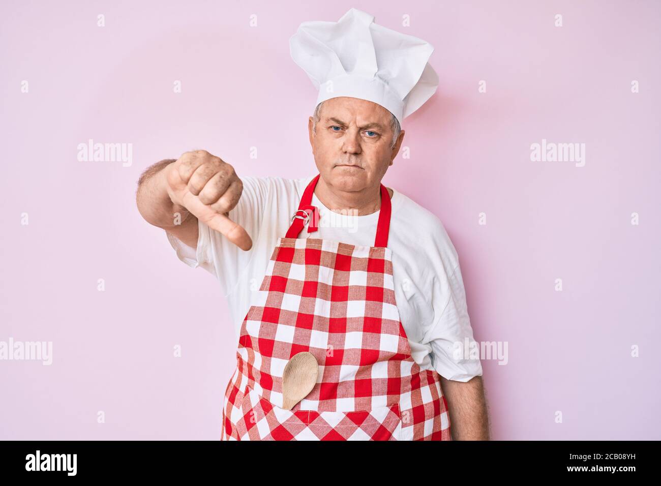 Senior grey-haired man wearing professional baker apron looking unhappy ...