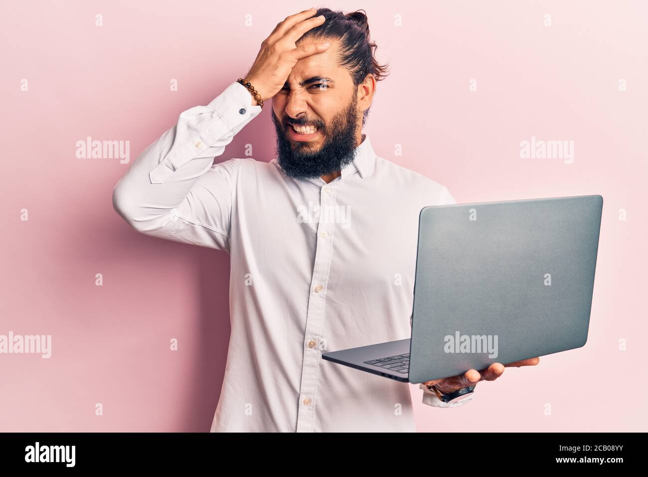 Young arab man holding laptop stressed and frustrated with hand on head ...