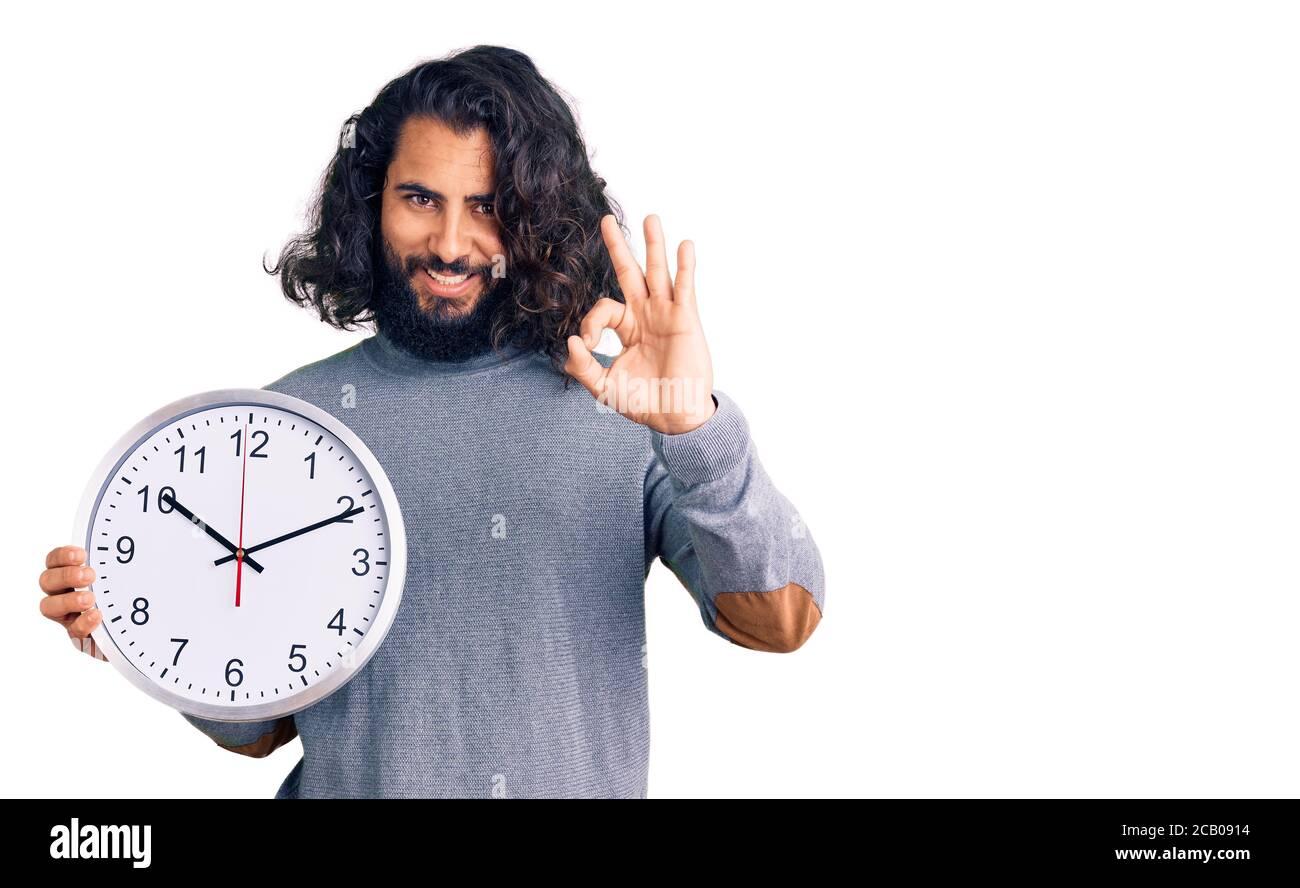 Young arab man holding big clock doing ok sign with fingers, smiling ...