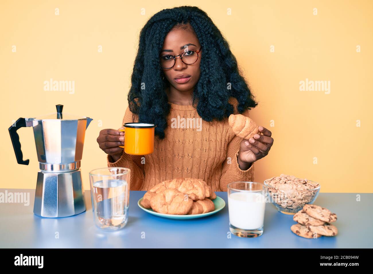 Young african american woman eating breakfast holding croissant ...