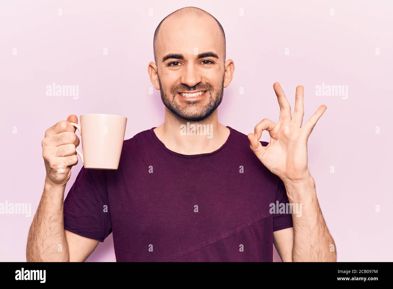 Young handsome bald man drinking cup of coffee doing ok sign with ...