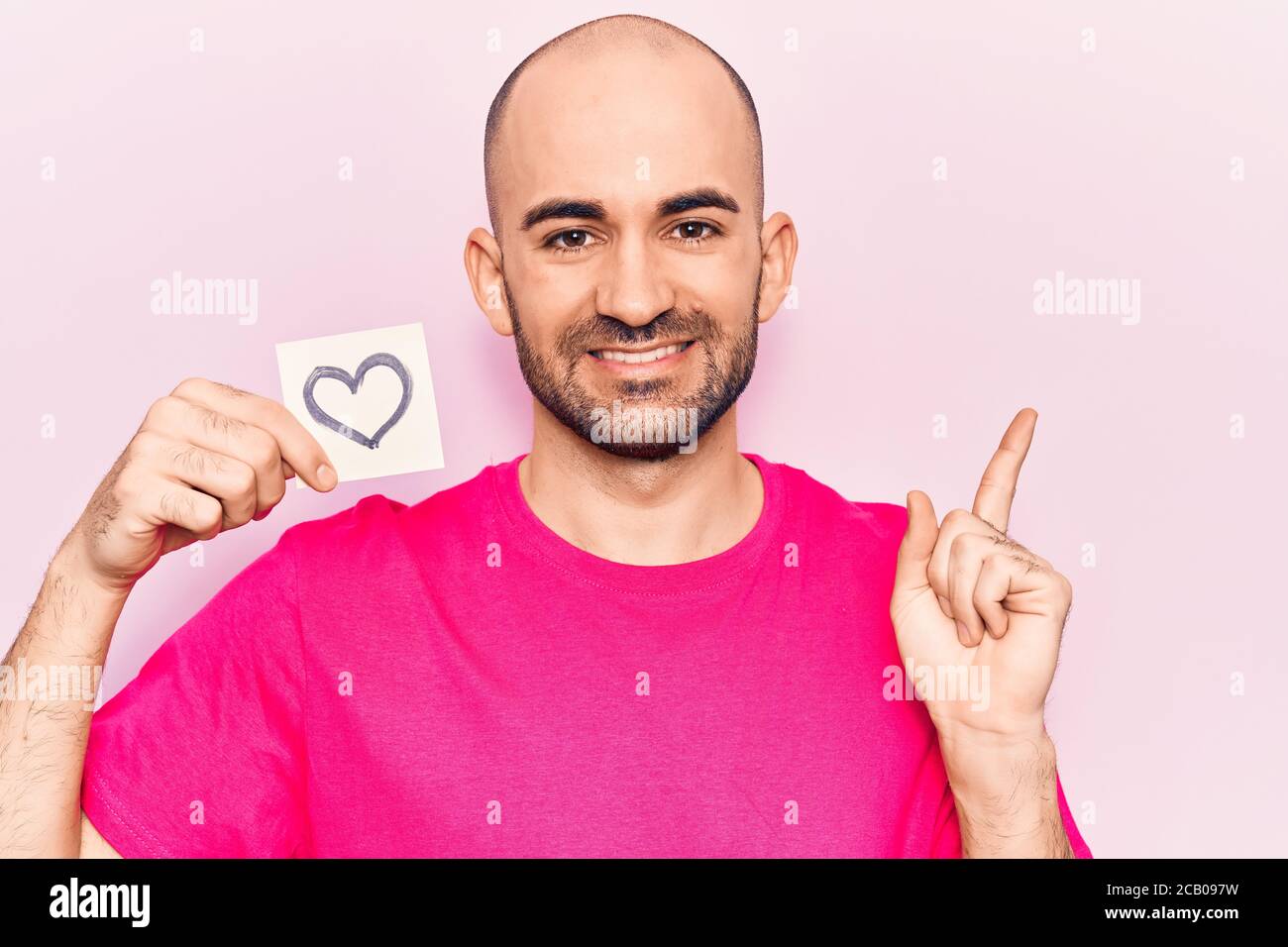 Young handsome bald man holding reminder with heart shape smiling happy ...