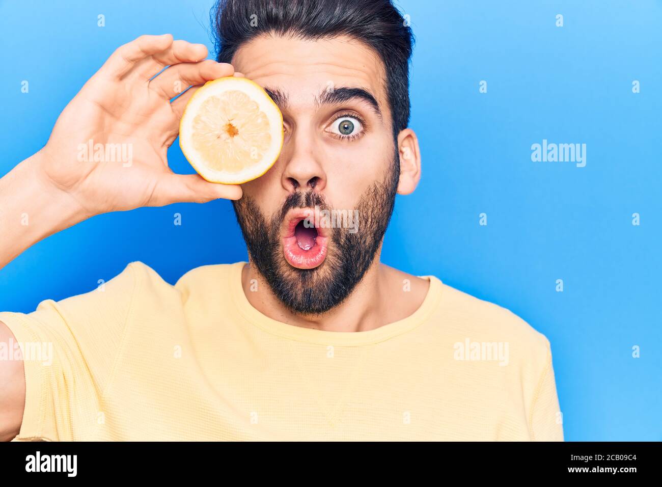 Young handsome man with beard holding slice of lemon over eye scared ...