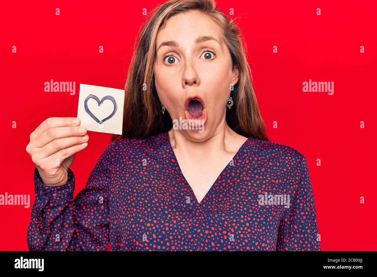 Young beautiful blonde woman holding paper with romantic heart scared ...