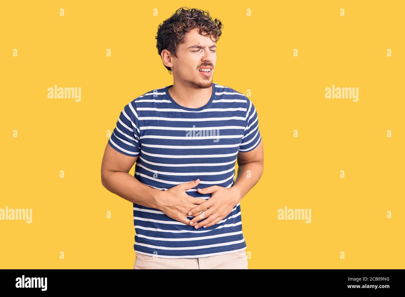 Young handsome man with curly hair wearing casual clothes with hand on ...