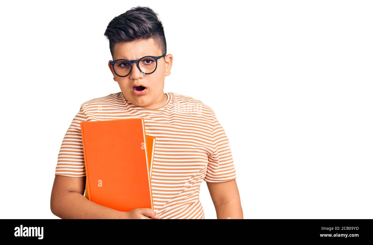 Little boy kid holding book wearing glasses in shock face, looking ...
