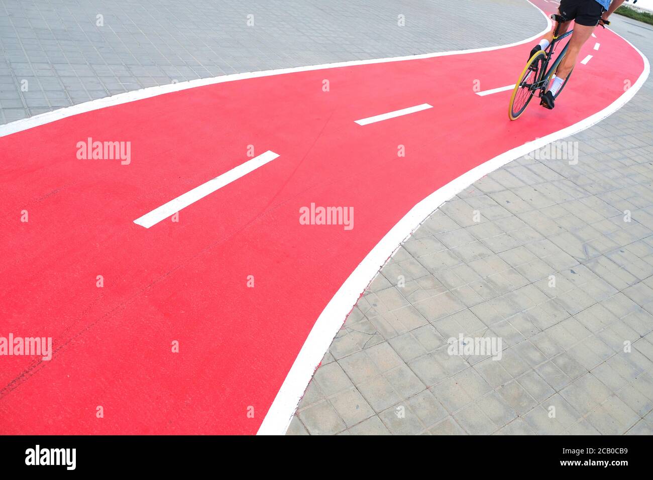 A red biking path in the city with a male figure of a biker moving away ...