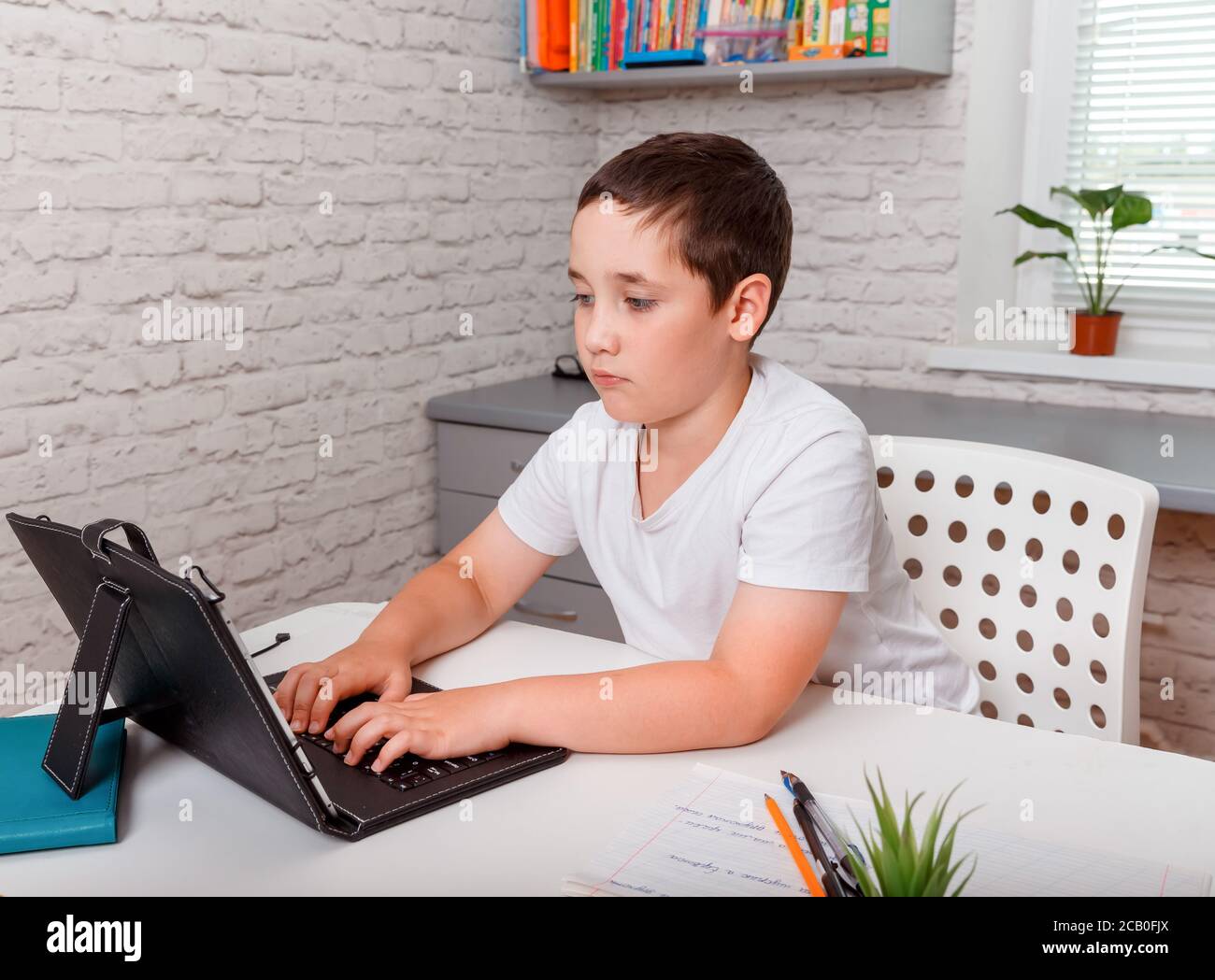 Schoolboy doing his homework in notebook with laptop computer at home ...