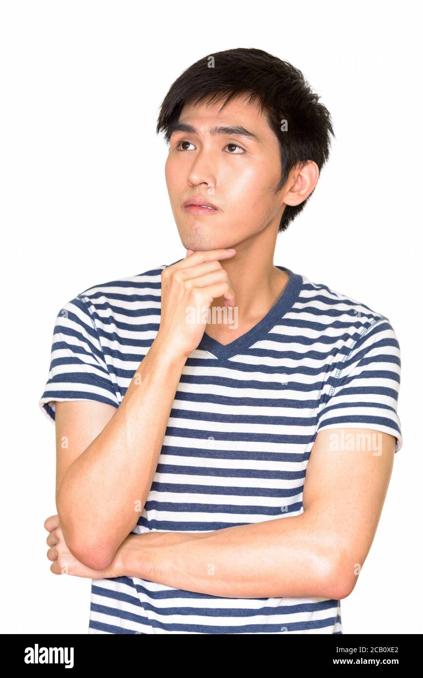 Studio shot of young handsome Asian man thinking against white ...