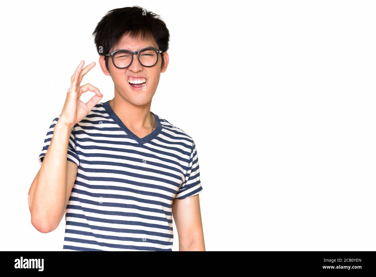 Studio shot of happy Asian nerd guy winking and making OK sign isolated ...