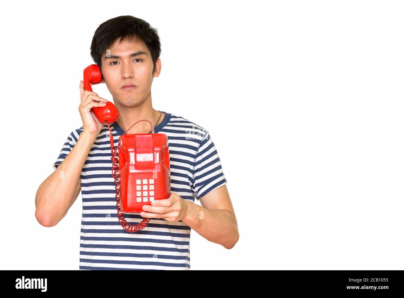 Studio shot of young handsome Asian man talking on phone isolated ...