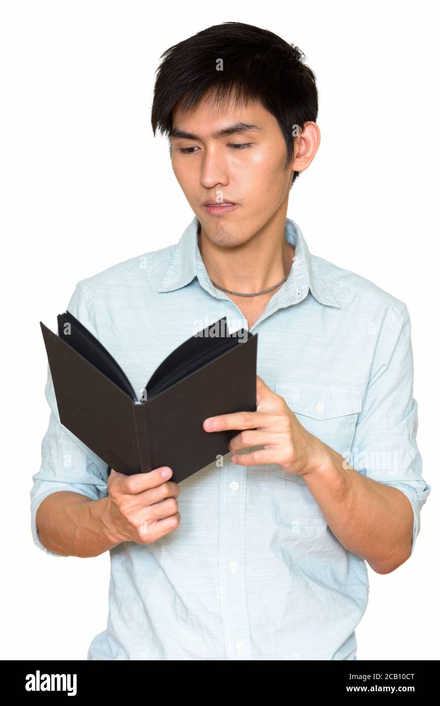 Studio shot of young Asian man reading book isolated against white ...