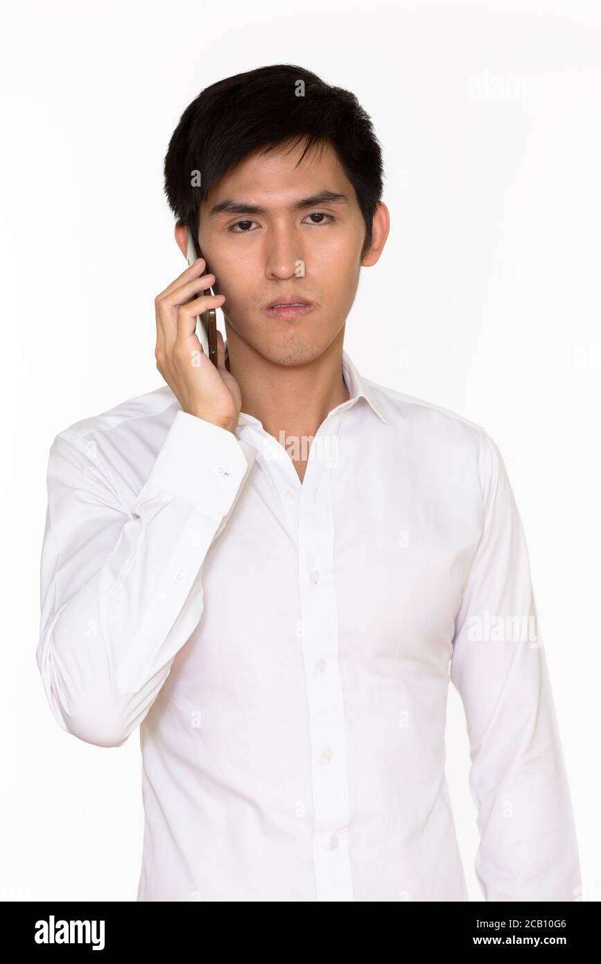 Studio shot of young handsome Asian man talking on mobile phone ...