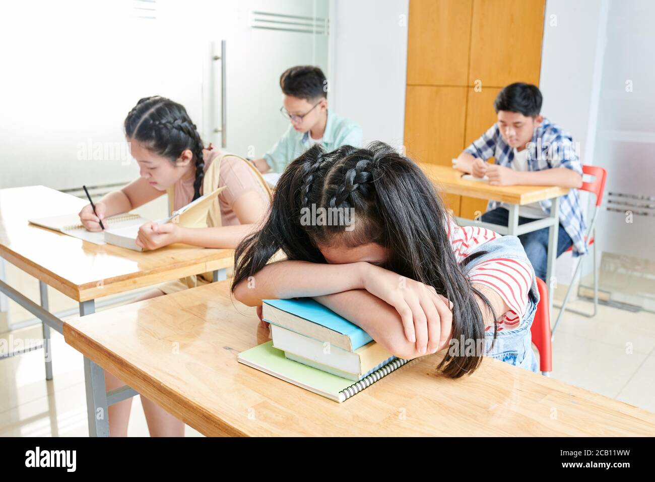 Tired girl leaning on students books, she and other shool students ...