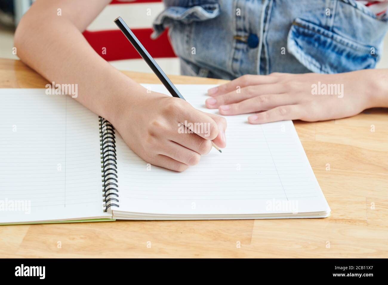 Close-up image of schoolgirl writing essay in copybook at her desk or ...