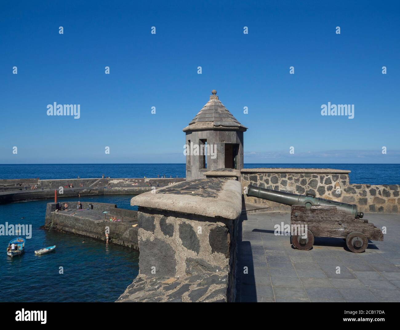old copper cannon on paved sea front with embrasure tower, stone wall ...