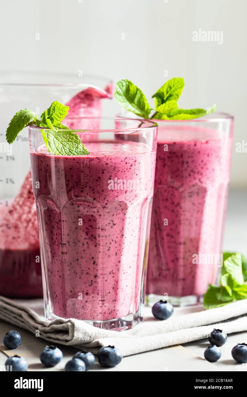Two glasses of blueberry smoothie with mint garnish on the table. Close ...