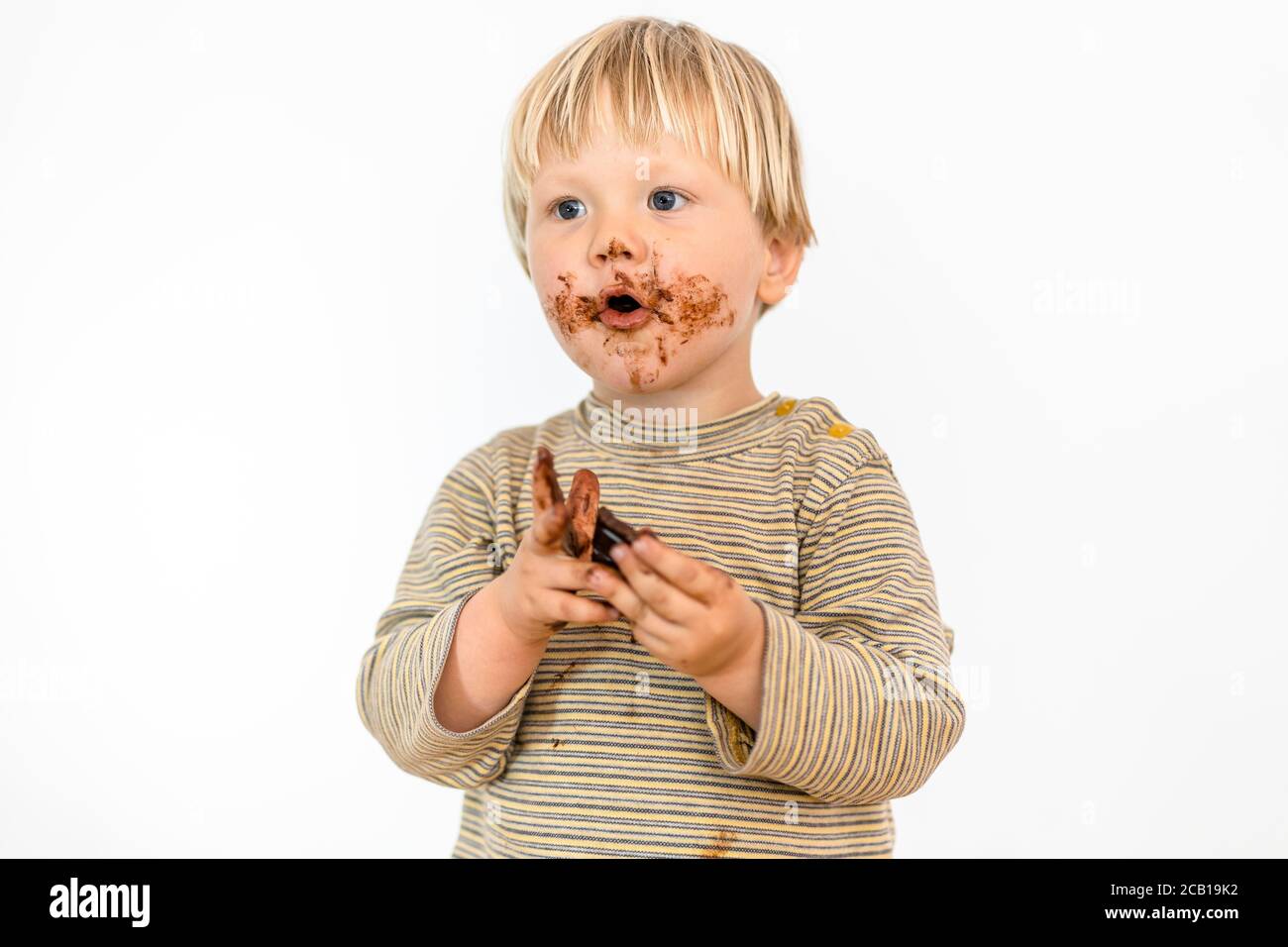 Cute blond toddler eating chocolate bar with great pleasure, white ...