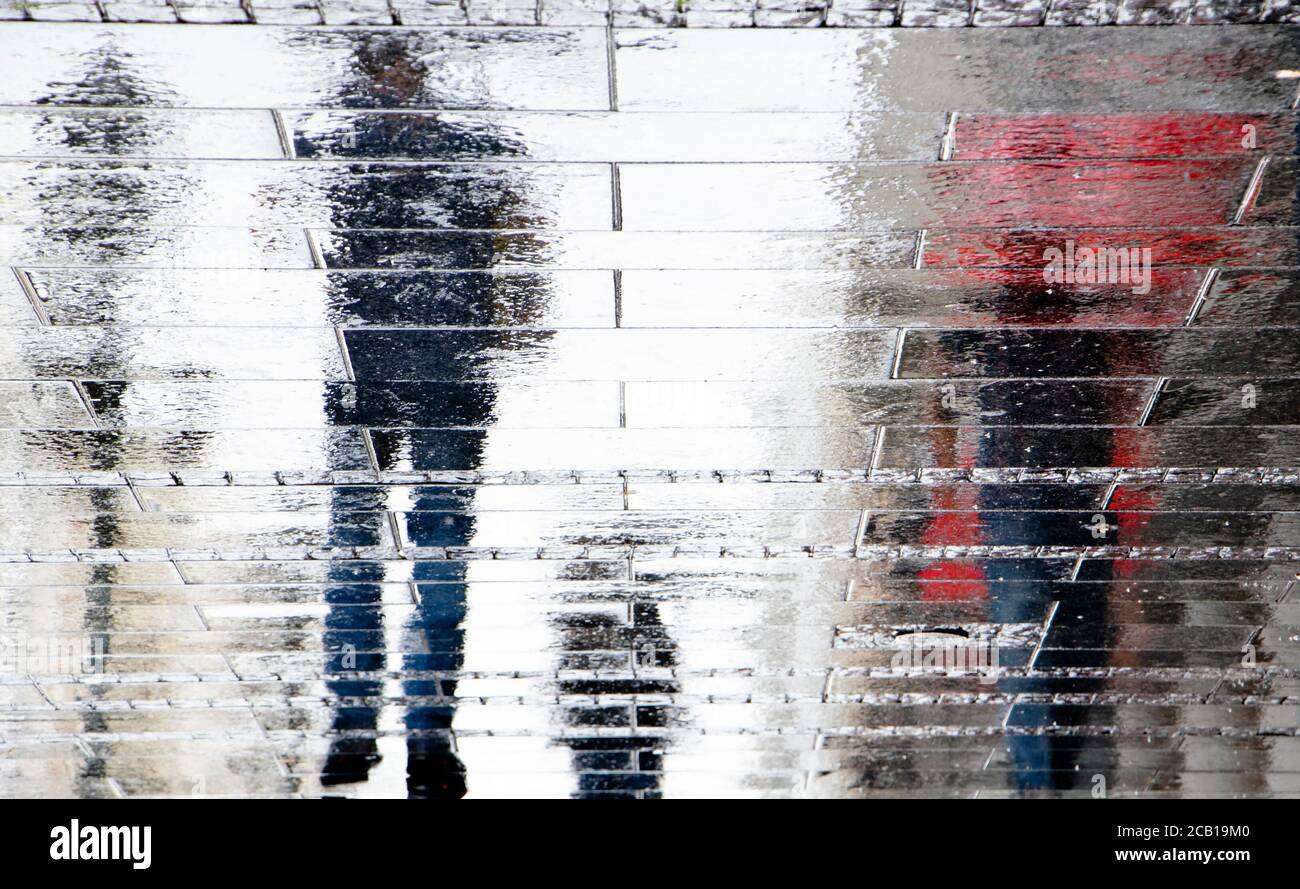 Blurry reflection shadow silhouette on wet puddle of people walking a ...