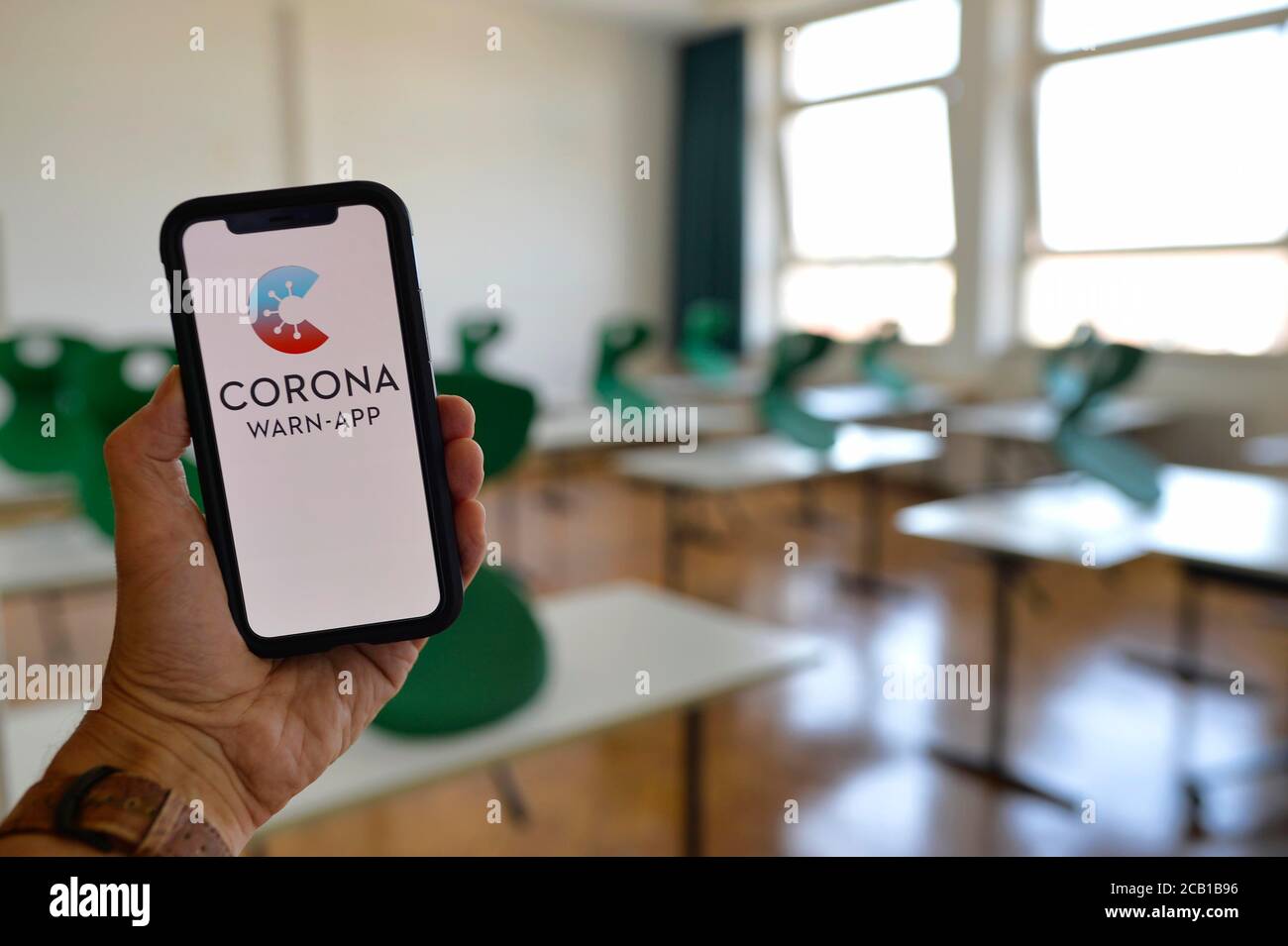 Hand holding smartphone with Corona Warning App in the classroom ...
