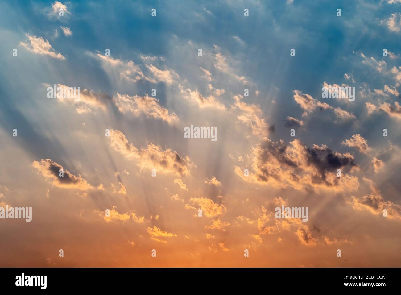 Sun rays breaking through clouds in a dramatic blue sky with sunset ...