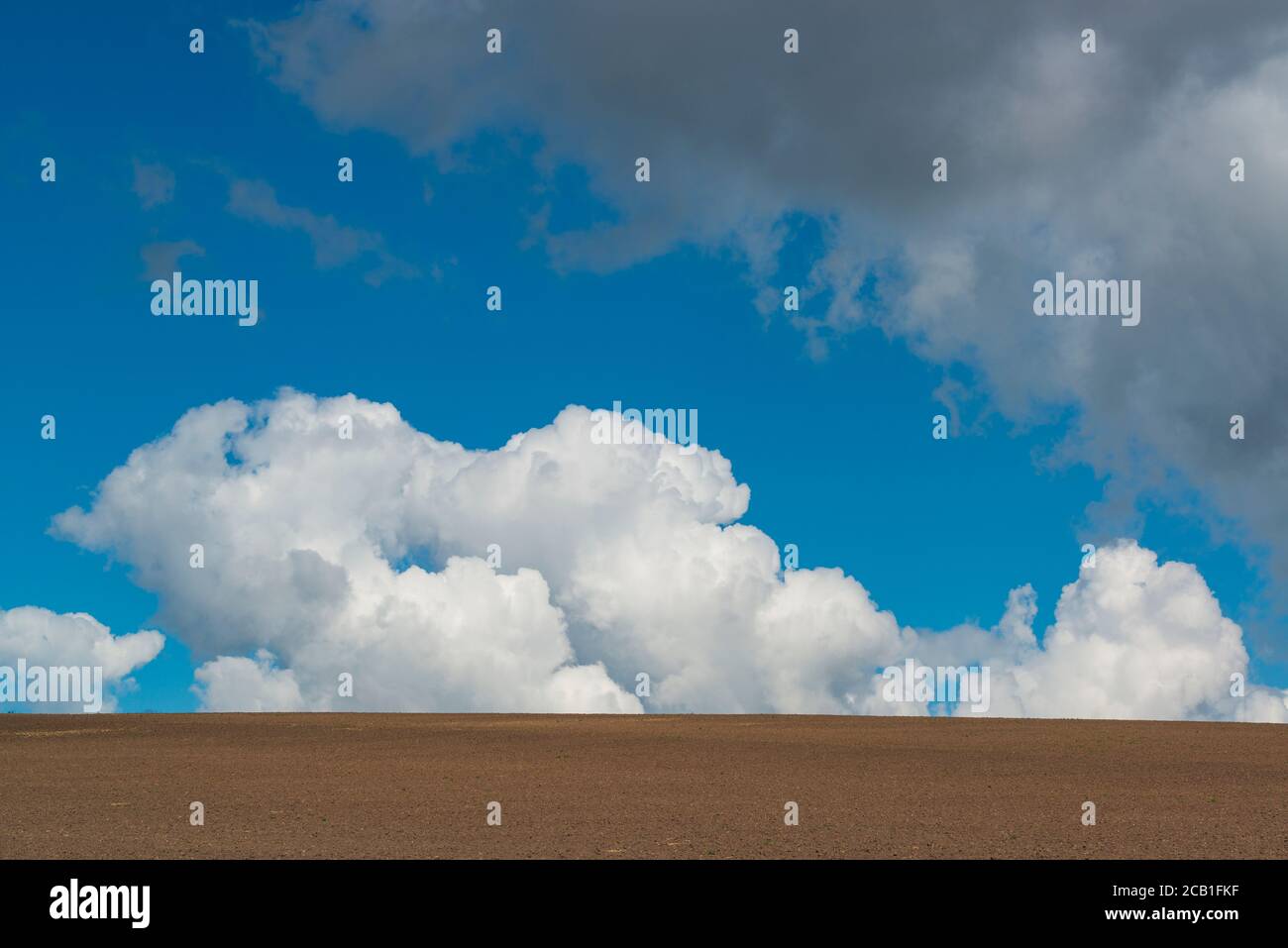 Minimalistic landscape with plowed soil and blue sky with big fluffy ...