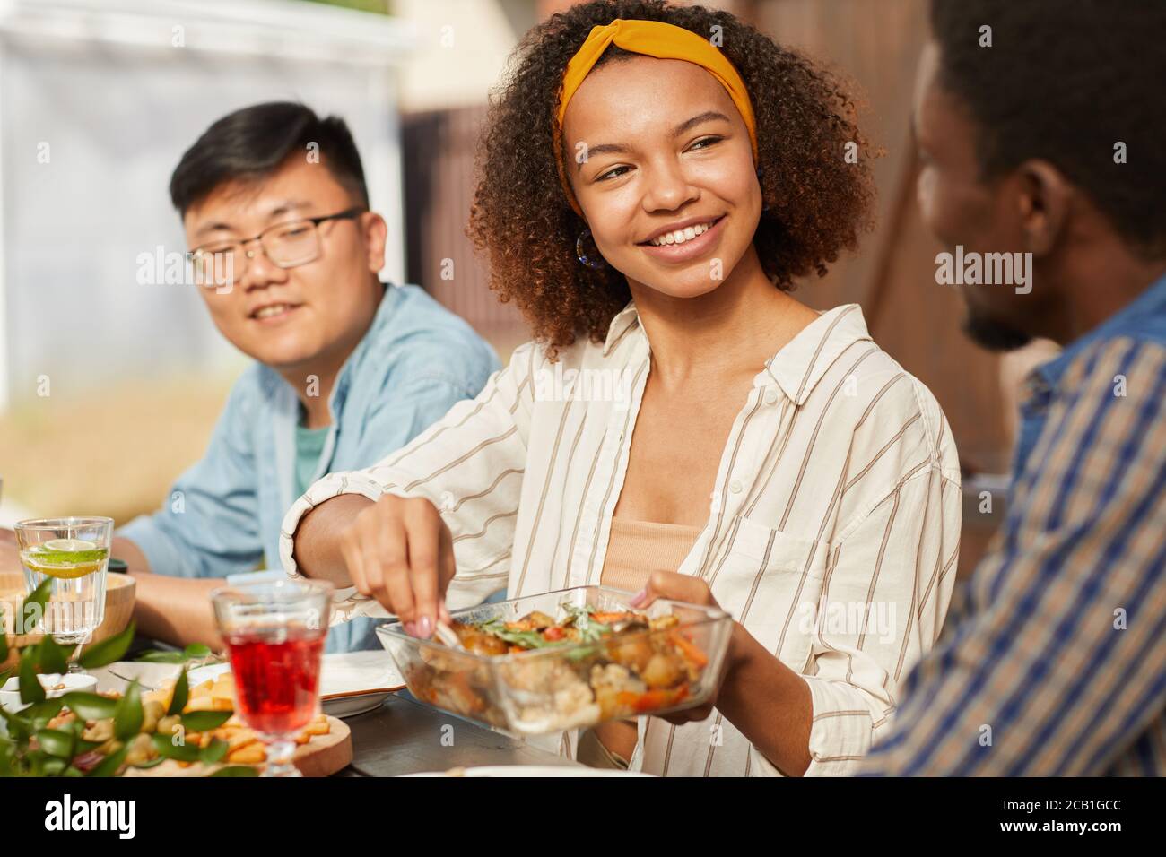 Portrait of smiling African-American woman sharing food while enjoying ...