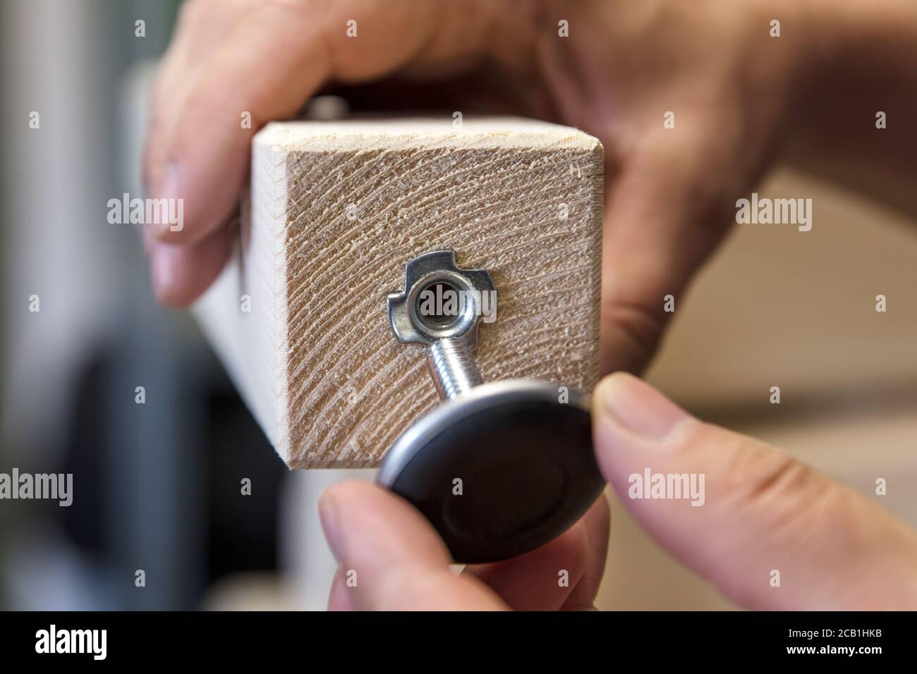 Man is installing a adjustable variable screw in a wooden desk or table ...