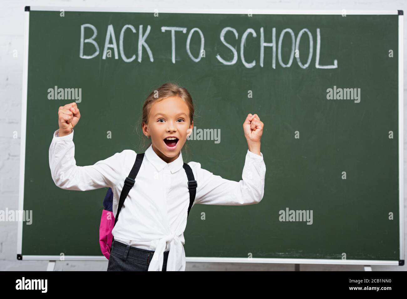 excited schoolgirl showing winner gesture near chalkboard with back to ...