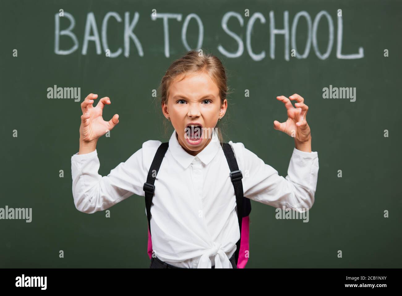 selective focus of angry schoolgirl showing scaring gesture near ...