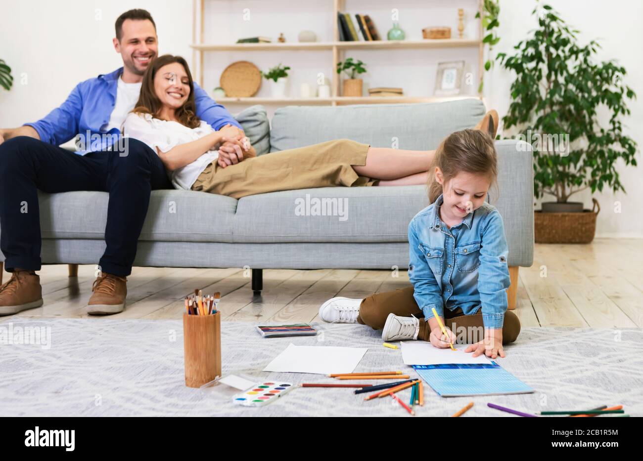 Parents Relaxing While Their Little Daughter Drawing Sitting At Home ...