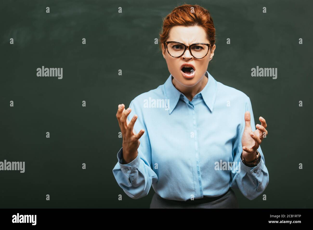 aggressive teacher in eyeglasses gesturing and yelling near chalkboard ...