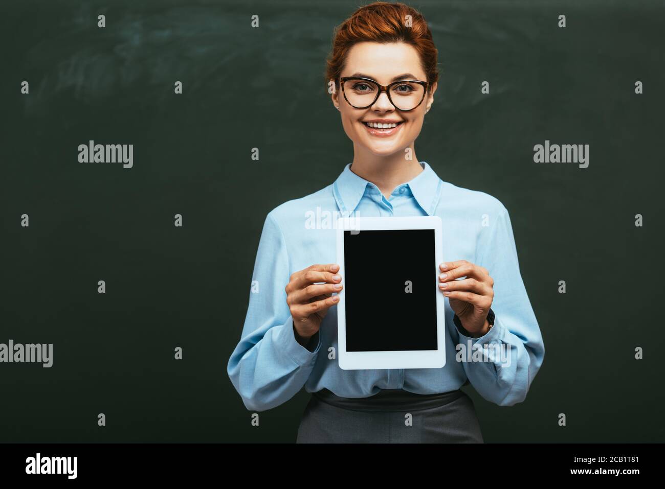 cheerful teacher showing digital tablet with blank screen while ...