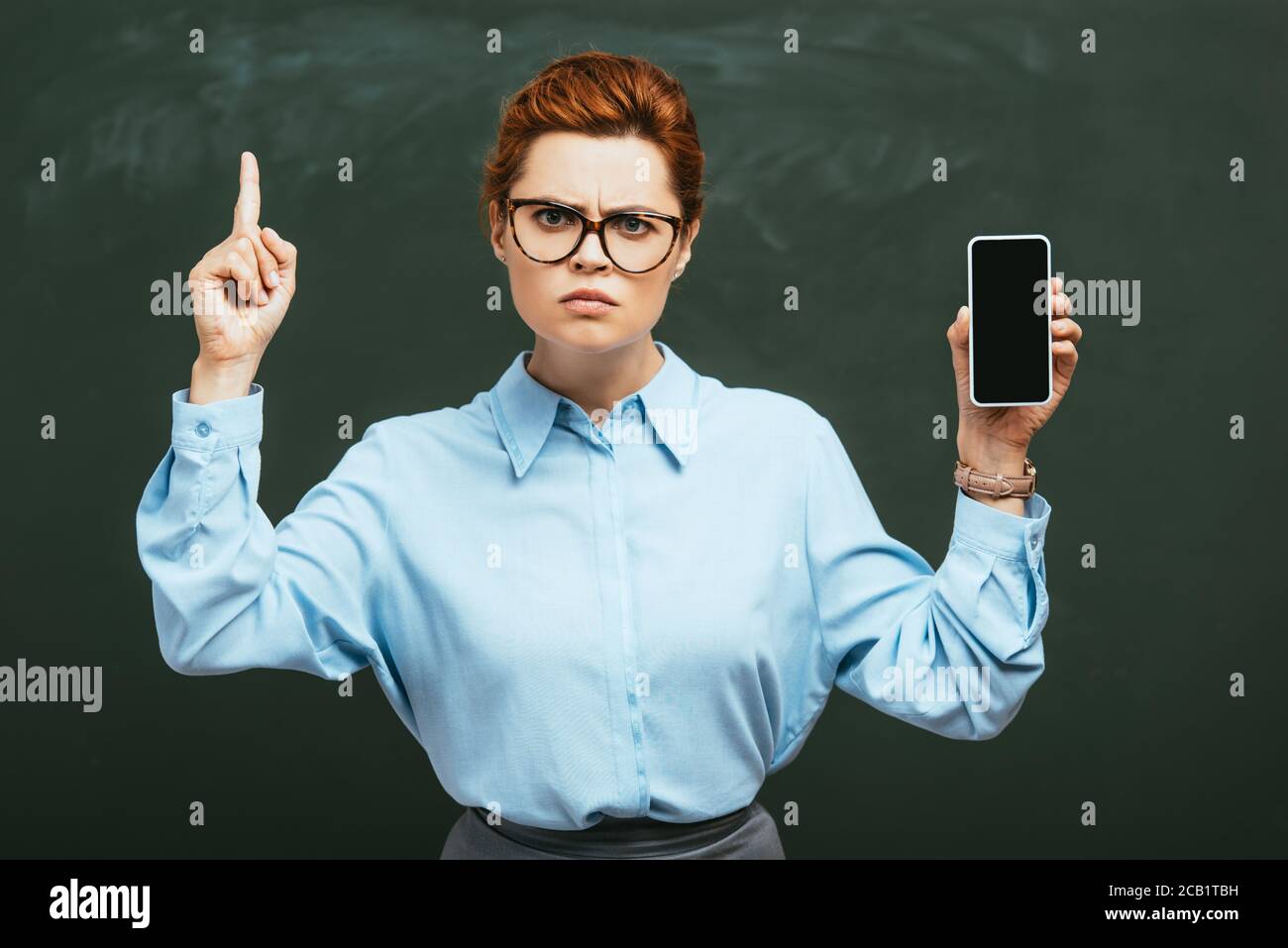 strict teacher showing attention gesture while showing smartphone with ...