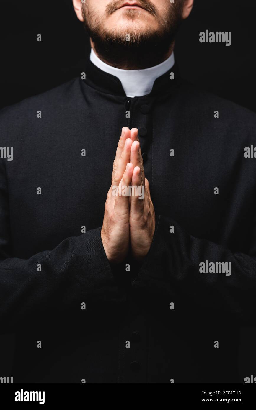 cropped view of priest with praying hands isolated on black Stock Photo ...