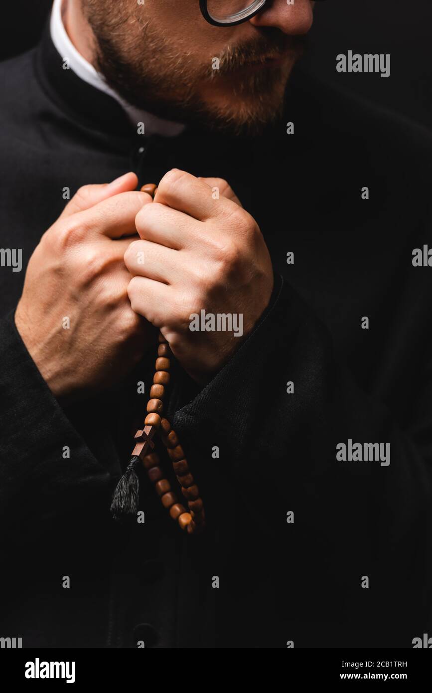 cropped view of bearded priest holding rosary beads in hands and ...
