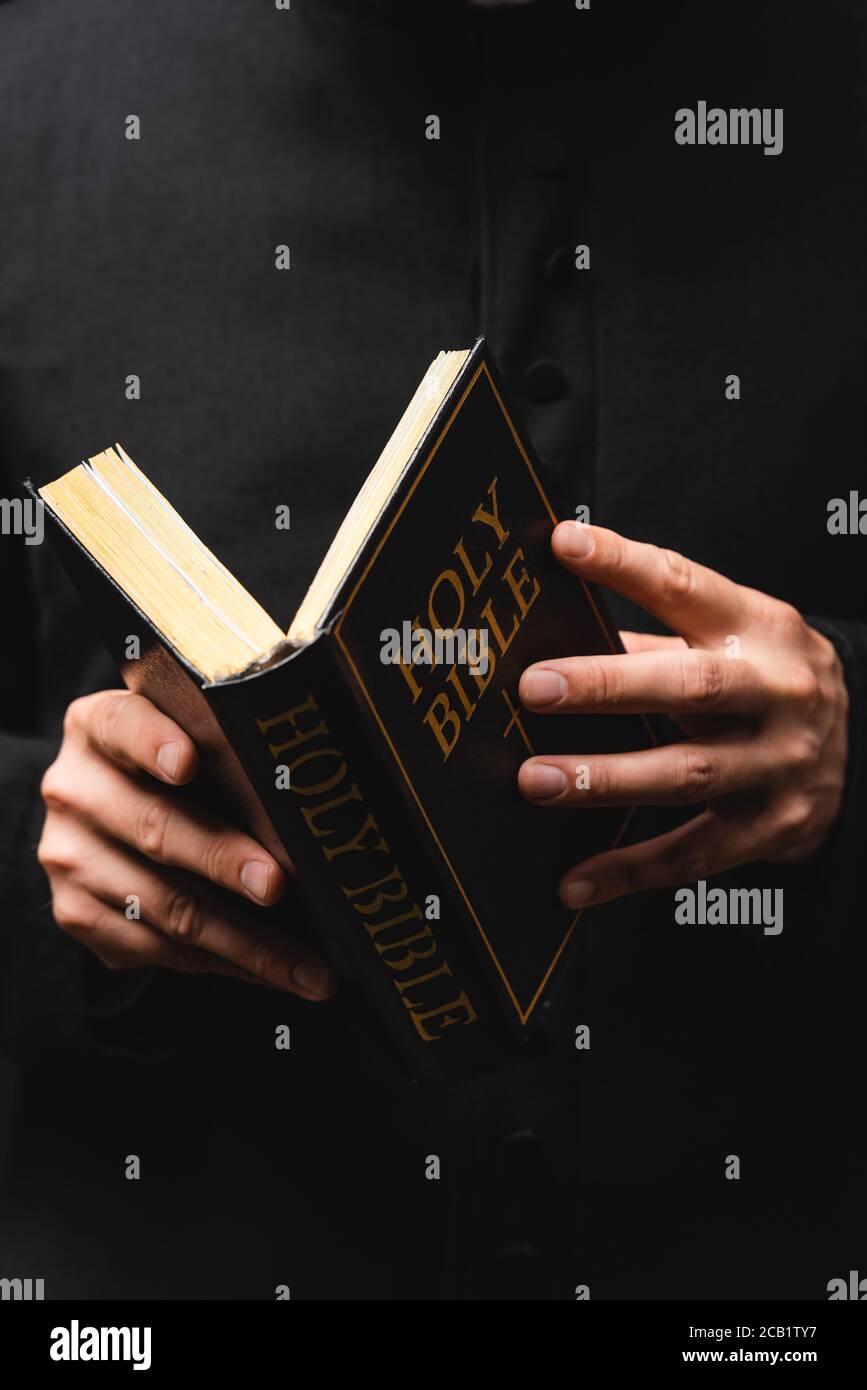 partial view of pastor reading holy bible isolated on black Stock Photo ...