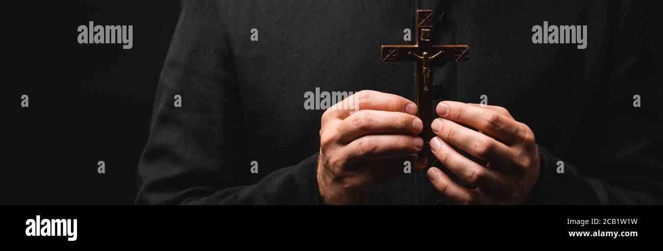 panoramic crop of pastor holding wooden cross isolated on black Stock ...