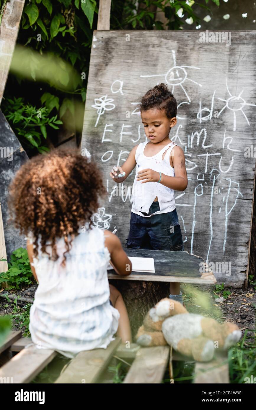 selective focus of poor african american kid standing near chalkboard ...