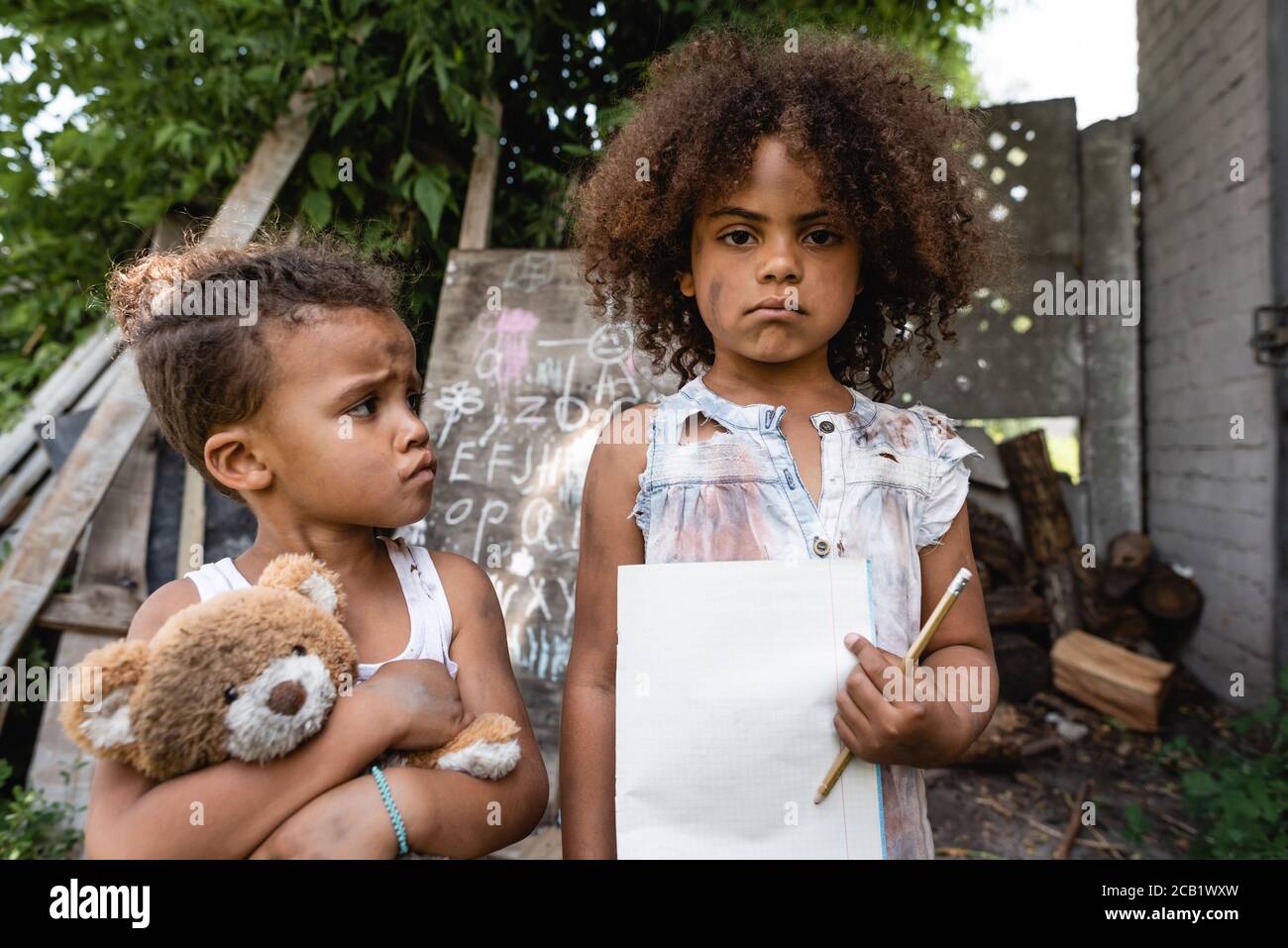 sad and poor african american kid holding blank paper and pencil near ...
