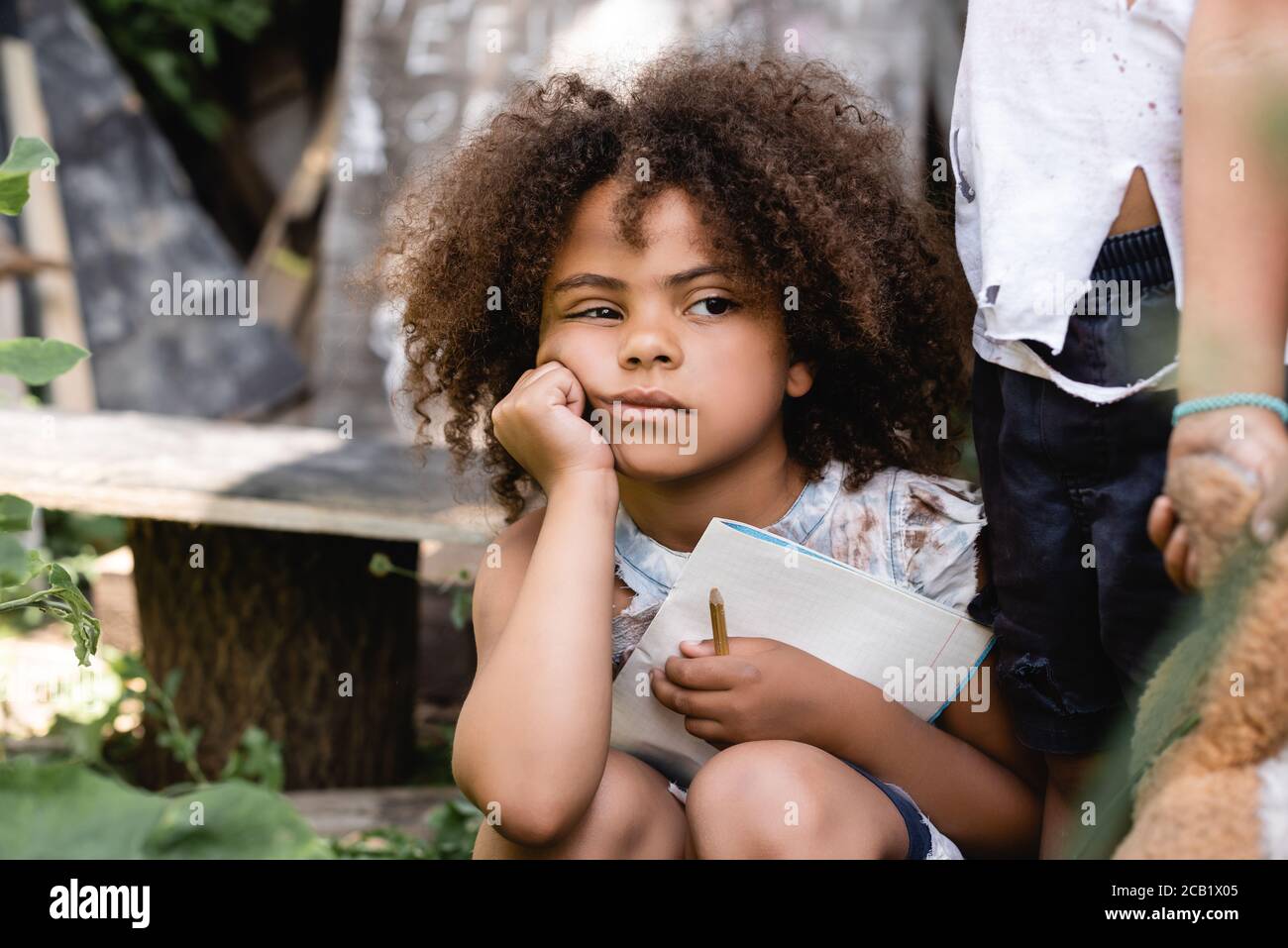 poor african american kid holding notebook near child standing with ...